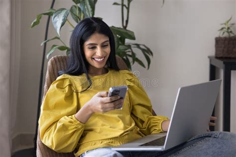 Smiling Woman Using Smartphone Seated In Cozy Armchair With Laptop Stock Image Image Of