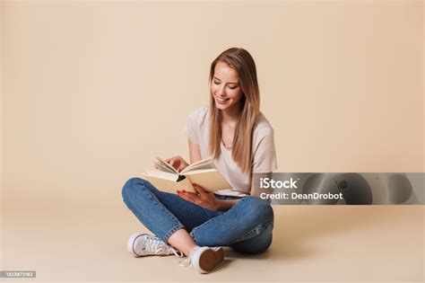 다리를 건너 고 흥미로운 책을 읽고 바닥에 앉아 있는 동안 캐주얼 한 옷을 입고 예쁜 젊은 여성의 사진 베이지 색 배경에 고립 책에 대한 스톡 사진 및 기타 이미지 Istock