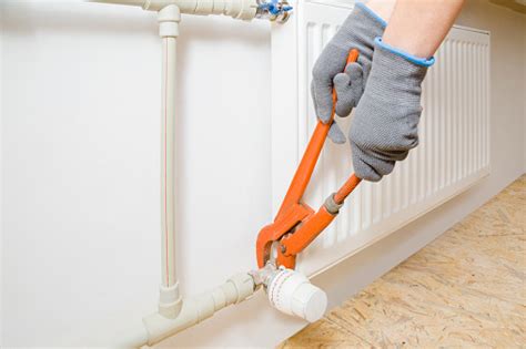젊은 성인 남자는 흰색 라디에이터를위한 오렌지 금속 조절 렌치와 나사 파이프 밸브를 사용하여 보호 장갑에 손을 집에서 열을