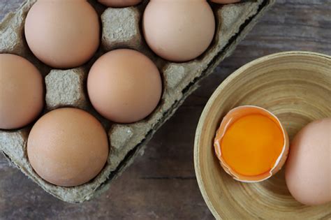 노른자 스튜디오 샷 높은 시야를 보여주는 계란을 포함하는 그릇 옆에 갈색 닭 계란의 배치를 포함하는 나무 테이블 상단에 열린 갈색 골판지 계란 상자의 클로즈업 이미지 0명에