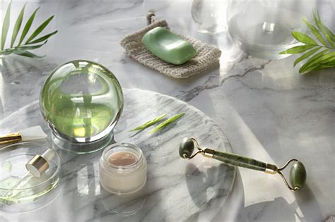 대리석 돌 배경에 녹색 옥 얼굴 롤러 마사지 및 얼굴 관리 제품 유리 크리스탈 볼과 이국적인 야자수 잎 수건 스킨케어 강장제 에센셜 오일 세럼 건강관리와 의술에 대한 스톡