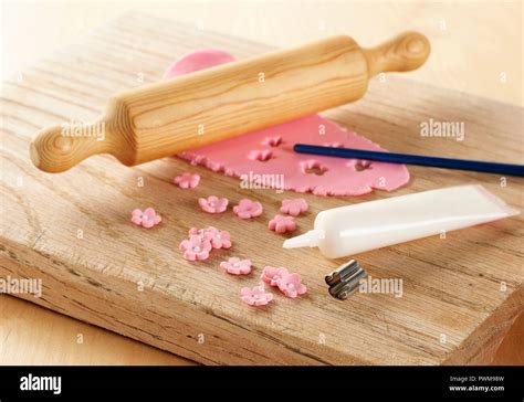 Pink Icing Rolled Out On A Board With Rolling Pin Showing A Metal Flower Cutter And White Icing
