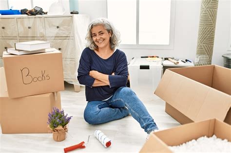 회색 머리카락을 가진 중년 여성이 새로운 집에서 바닥에 앉아 카메라를 바라 보는 교차 된 팔로 웃고있는 행복한 얼굴 긍정적 인 사람 라틴 아메리카 히스패닉 민족에 대한 스톡