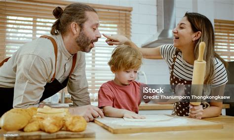 아버지와 어머니는 아기 아들이 집에 있는 부엌 카운터에서 반죽을 반죽하는 것을 가르친다 부모와 소년 아이는 실내 활동을 함께 즐기고 재미있게 요리합니다 3 명에 대한 스톡