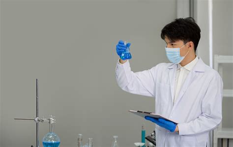 젊은 아시아 과학자는 클립보드를 들고 있는 동안 에렌마이어 플라스크에서 푸른 액체 화학 물질을 보고 코로나바이러스 질환 2019 실험실에서 Omicron 균주 테스트 과정