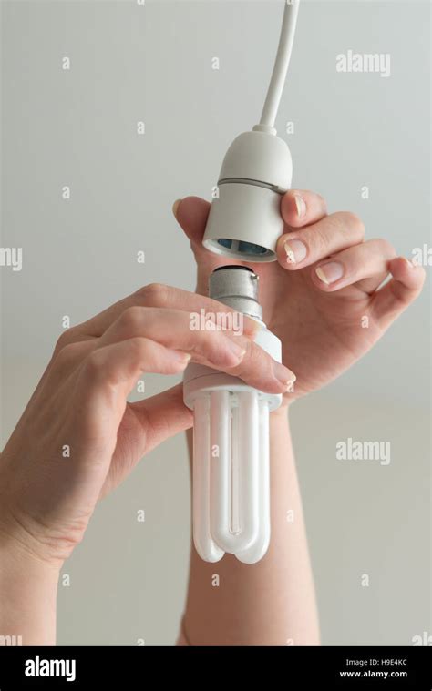 Hands Fit Or Remove An Energy Saving Light Bulb From A Hanging Ceiling Mount In A White Room