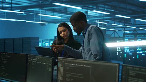 Coworking Technicians Looking At Laptop Screen Working In Data Center Ensuring Optimal