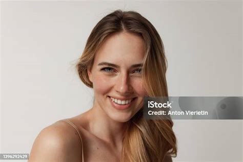 카메라에 미소 짓는 완벽한 얼굴을 가진 부드러운 젊은 여성의 초상화 회색 스튜디오 배경 위에 고립 된 포즈를 취하십시오 자연미