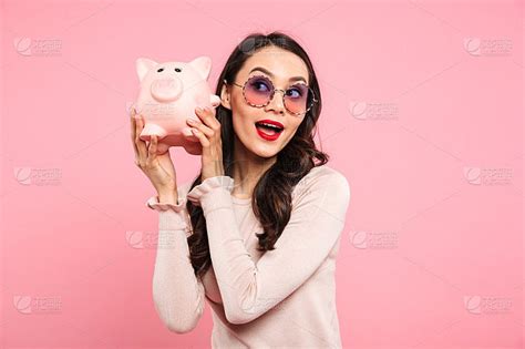 可爱的女人20岁的形象长长的黑发戴着少女眼镜拿着储蓄罐孤立在粉红色的背景
