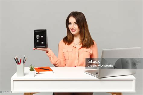 돈 축적에 대 한 안전 금속 은행을 들고 젊은 예쁜 여 자가 회색 배경에 고립 된 Pc 노트북과 화이트 데스크에서 작업을 앉아 성취 비즈니스 커리어 라이프 스타일 컨셉 복사