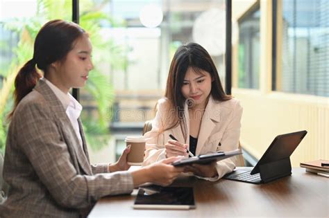 Smiling Asian Female Colleagues Using Digital Tablet And Analyzing Financial Data At Co Working