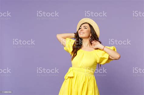 노란 드레스에 행복 한 젊은 여자의 초상화 여름 모자를 찾고 파스텔 바이올렛 벽 배경에 고립 된 머리에 손을 넣어 사람들은 진심으로 감정 라이프 스타일 개념입니다 복사
