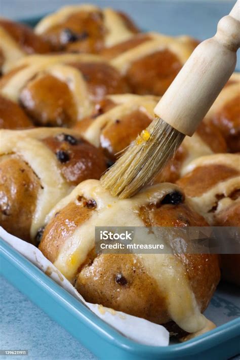 갓 구운 수제 부활절 핫 크로스 만두의 클로즈업 이미지 그리스 방지 양피지 종이에 붙어있는 비 스틱 베이킹 오븐 트레이 패스트리 브러시를 사용하여 살구 잼 홈 베이킹
