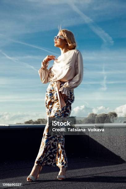 실크 블라우스 인쇄 된 바지 선글라스를 착용하고 지붕에 교차 된 다리를 들고 서있는 긴 공정한 머리카락을 가진 젊은 여성 패션모델에 대한 스톡 사진 및 기타 이미지 Istock