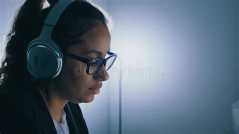 Young Female Programmer With Headphones Working Intensely In A Dimly Lit Office Illuminated By