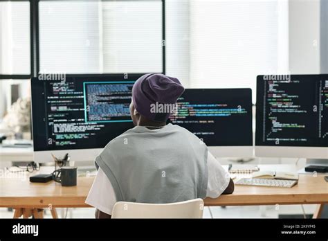 Back View Of Young Software Developer Sitting By Workplace In Front Of
