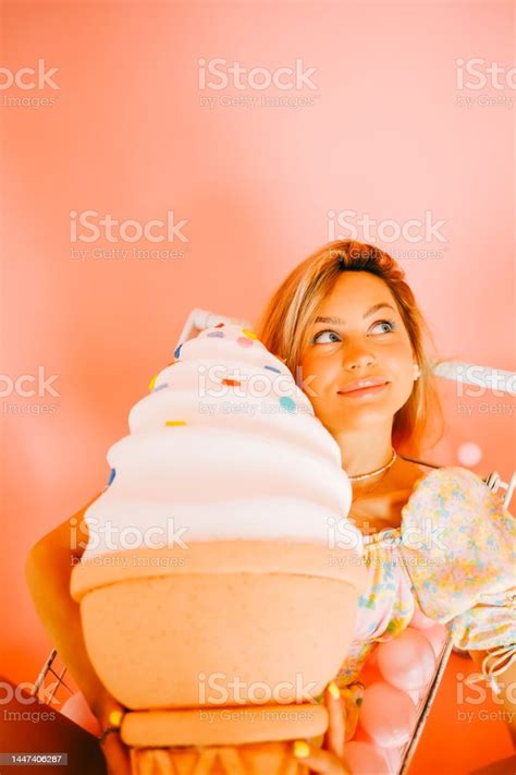 과자와 사탕의 인물이 있는 분홍색 배경에 큰 아이스크림을 먹고 있는 쇼핑 카트에 금발 머리를 가진 쾌활한 매력적인 백인 여성 패션 모델 가냘픈에 대한 스톡 사진 및 기타
