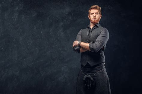 우아한 조끼를 입은 빨간 머리 남자 넥타이와 킬트 포즈와 함께 그의 팔은 어두운 질감의 벽에 스튜디오에서 교차 남자에 대한 스톡