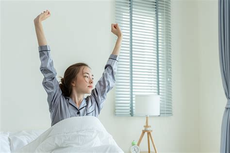 잠옷을 입은 아름다운 백인 소녀가 아침에 일어나서 목을 졸라매고 있습니다 매력적인 젊은 여성은 웃고 행복감을 느끼고 집에서 침실에서 침대에서 자고 나서 몸을 스트레칭합니다