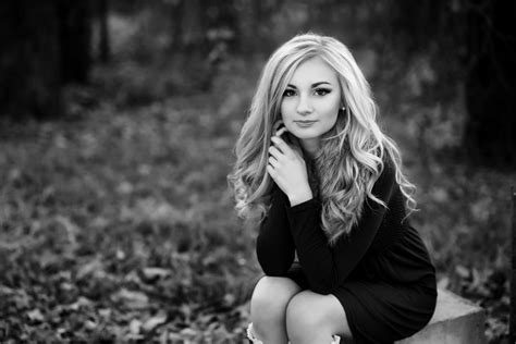 Black And White Photo Of A Woman Sitting On A Log In The Woods With Her Hand Under Her Chin