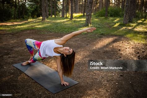 한 젊은 여성이 숲 한가운데서 요가를 하면서 자연과 깊은 교감을 느끼는 순간을 경험한다 태양 광선이 두꺼운 나무 꼭대기를 통과합니다 30 34세에 대한 스톡 사진 및 기타