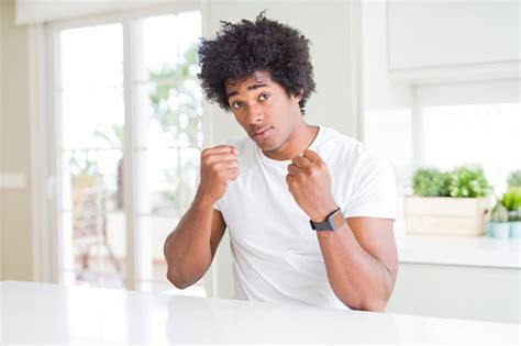 집에 앉아 캐주얼 흰색 티셔츠를 입고 젊은 아프리카 계 미국인 남자 주먹 방어 제스처 화가 와 화가 얼굴 문제를 두려워 와 싸울 준비 T 셔츠에 대한 스톡 사진 및 기타