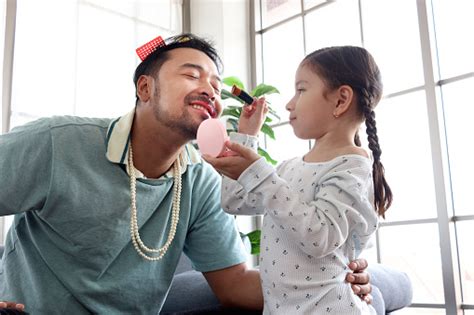 작은 사랑스러운 딸과 함께 노는 즐거운 아버지 화장품으로 아빠에게 화장을하는 소녀 거실의 소파에 앉아있는 소녀 가족 휴가 주말에 재미 있고 서있는 시간을 갖습니다 2명에