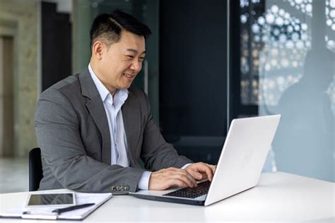 노트북을 사용하여 사무실에서 일하는 성공적인 성숙한 아시아인 키보드로 타이핑하고 웃는 남자 일과 성취 결과에 만족하는 사업가 직장에서 프로그래머 35 39세에 대한 스톡