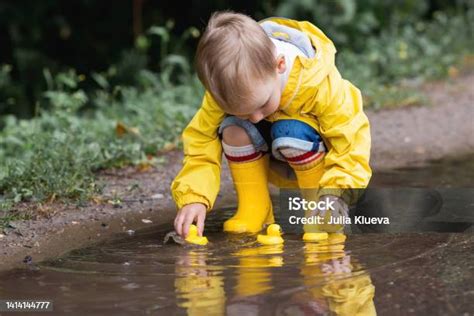무지개 양말 노란 고무 부츠 재킷을 입은 어린 아이가 웅덩이를 뛰어 넘어 노란 고무 오리와 놀고 있습니다 여름과 가을 휴가의