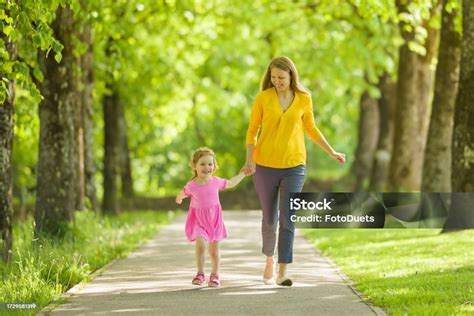 행복한 웃는 어린 딸과 젊은 성인 어머니가 나무 골목 공원의 보도에서 달리고 있다 아름답고 따뜻하고 화창한 여름날에 함께 시간을 보냅니다 정면도 아이에 대한 스톡 사진 및