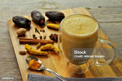 심황 라떼와 나무 배경에 대한 도마에 누워 있는 재료가 있는 유리 머그잔의 전경 심황 뿌리 대추 계피 스틱 육두구 카다몬 포드 스타 아니스 및 정향 0명에 대한 스톡 사진