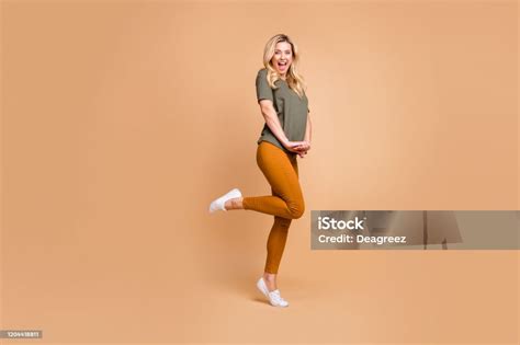 전체 길이 프로필 사진 의 놀라운 금발 의 아가씨 슬림 완벽한 모양 거리 여름 룩 꼬리 치는 흥분 분위기 착용 녹색 티셔츠 바지 고립 된 베이지 색 배경 바지 의복에 대한