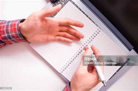 체크 셔츠를 입은 남성의 손은 흰색 펜을 들고 노트북에 쓰고 있습니다 종이 노트북에 아이디어 메모 작업 계획을 작성하는 손을 입력합니다 프리랜서 프로그래머 노트북에서