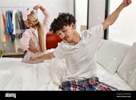 Young Beautiful Couple Yawning And Stretching Arms Sitting On The Bed