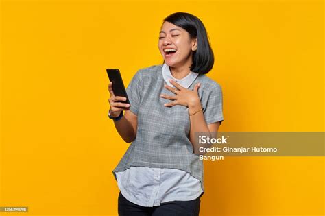 노란 배경에 입을 벌리고 휴대 전화를 들고 있는 쾌활한 젊은 아시아 여성 행복에 대한 스톡 사진 및 기타 이미지 행복 스튜디오 촬영 여자 Istock