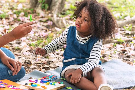 작은 곱슬 머리 혼합 경주 소녀는 잎잔디에 앉아 공원에서 손 어머니에 플라스틱을보고 아이들은 부모가 정원에서 가르치는 동안 즐기고 행복과 함께 여름 활동을 여름 2 3 살에