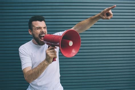 그것에 비명을 내는 손에 빨간 확성기를 들고 남자의 초상화입니다 또한 남자는 손가락으로 위쪽을 향하고 있습니다 줄무늬와 파란색 배경에 고립입니다 가능성에 대한 스톡 사진 및