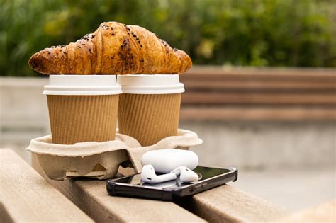 신선한 구운 초콜릿 크로와상은 차를 마실 수있는 뚜껑이있는 두 개의 종이컵에 있습니다 아침 식사 커피는 테이블에서 가져갑니다 갈색 종이컵 홀더가 있는 테이크아웃 커피 무선
