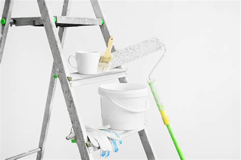 벽에 그림을 그리기 위한 도구 롤러 트레이 페인트 양동이 브러시 장갑 흰색 으로 칠해진 벽 근처의 사다리에 커피 한 잔 홈 리노베이션 기간 동안 커피 휴식 공간을 복사합니다