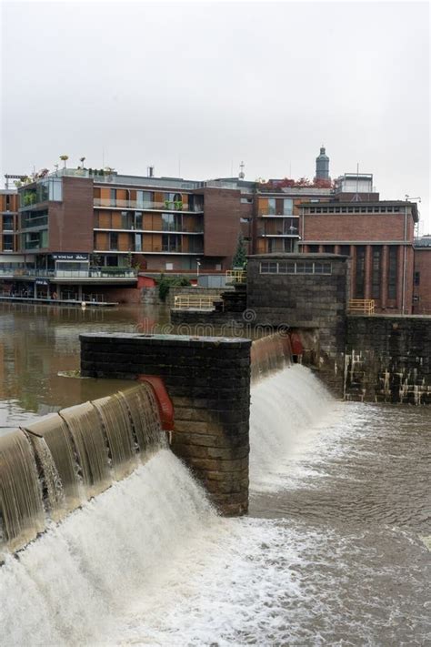 Waterfall Dam Flowing Through Concrete Barriers With Modern Buildings In The Background On A