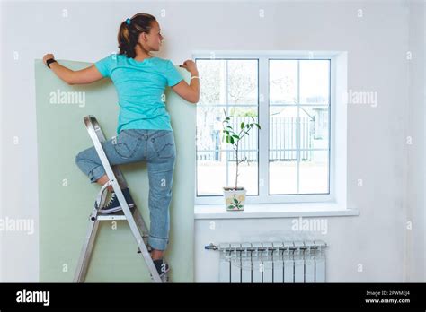 Woman In Jeans And Turquoise T Shirt Standing On Stepladder And Holding