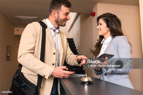 젊은 사업가 가 호텔에 체크인 태블릿에 그를 보여주는 호텔 카운터 뒤에 미소 여성 접수 호텔 리셉션에 대한 스톡 사진 및 기타