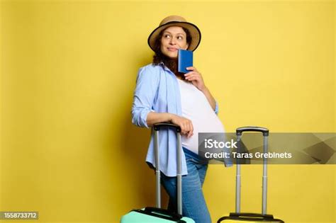유쾌한 임산부 여행자는 미소를 지으며 꿈결처럼 복사 공간을 옆으로 바라보며 노란색 배경에 여행 가방을 들고 포즈를 취한다 40주 태아에 대한 스톡 사진 및 기타 이미지