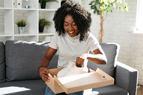 젊은 아프리카 여자는 온라인 구매와 함께 소포 골판지 상자의 포장을 풀기 집에서 소파에 앉아 20 24세에 대한 스톡 사진 및 기타 이미지 Istock