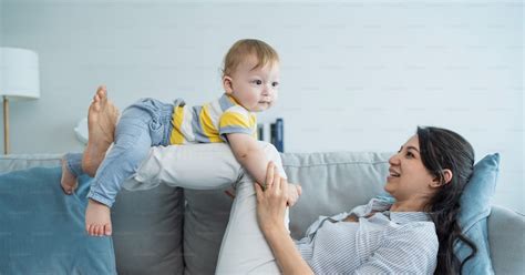 백인 사랑하는 엄마는 거실의 소파에서 아기 아이와 놀고 있습니다 행복한 가족 매력적인 아름다운 돌보는 젊은 어머니 들어 올리는 유아 아들이 집에서 아침에 비행기 게임을