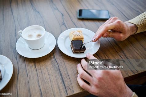 클로즈업 찻 숟가락을 들고 커피 브레이크에서 맛있는 초콜릿 케이크를 먹는 남자의 손 테이블 위의 복사 공간을위한 빈 화면이있는 스마트 폰 Brand Name Smart