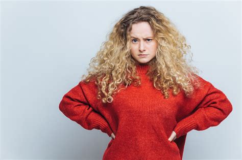 곱슬 머리를 가진 불쾌한 화가 여자의 사진 허리에 손을 유지 느슨한 스웨터를 입고 흰색 스튜디오 배경을 통해 고립 된 불일치를 표현한다 사람과 부정적인 감정 개념 곱슬