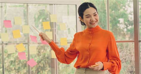 비즈니스 사람들은 사무실의 프로젝트 계획 보드에서 일하고 동료 친구와 대화하여 프로젝트 개발을 분석합니다 그들은 유리 벽에 게시 된 스티커 메모를 사용하여 정리합니다