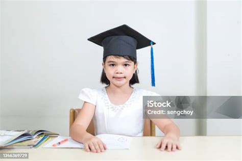 쾌활한 아시아 의 어린 소녀 학생의 초상화는 박격포 또는 졸업 모자를 착용하고 연필을 잡고 복사 공간이있는 흰색 배경이있는 노트북에 씁니다 교육 졸업 개념 스톡 사진 개념에