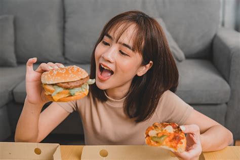 패스트 푸드 테이크 아웃 집으로 돌아갑니다 테이크 아웃 및 배달 시 햄버거를 먹는다 거실에서 아시아 여성의 라이프 스타일 사회적 불변과 새로운 정상 먹기에 대한 스톡 사진